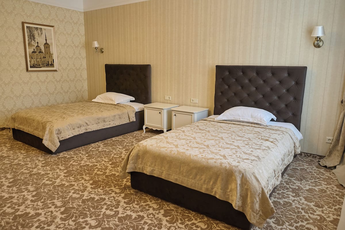 Quarto de hotel com duas camas, uma cabeceira grande, uma mesa de cabeceira e uma luminária fixada na parede.