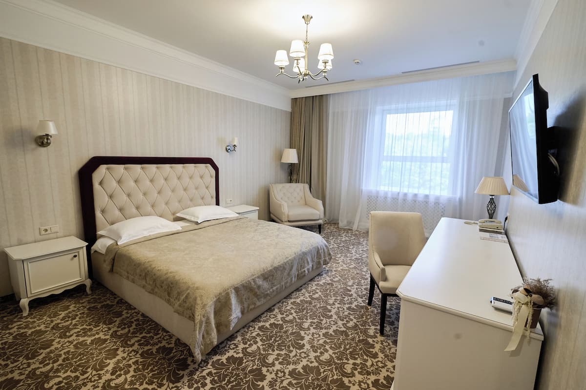 Quarto de hotel com uma cama grande, uma escrivaninha, uma cadeira, uma televisão e uma janela com cortinas.