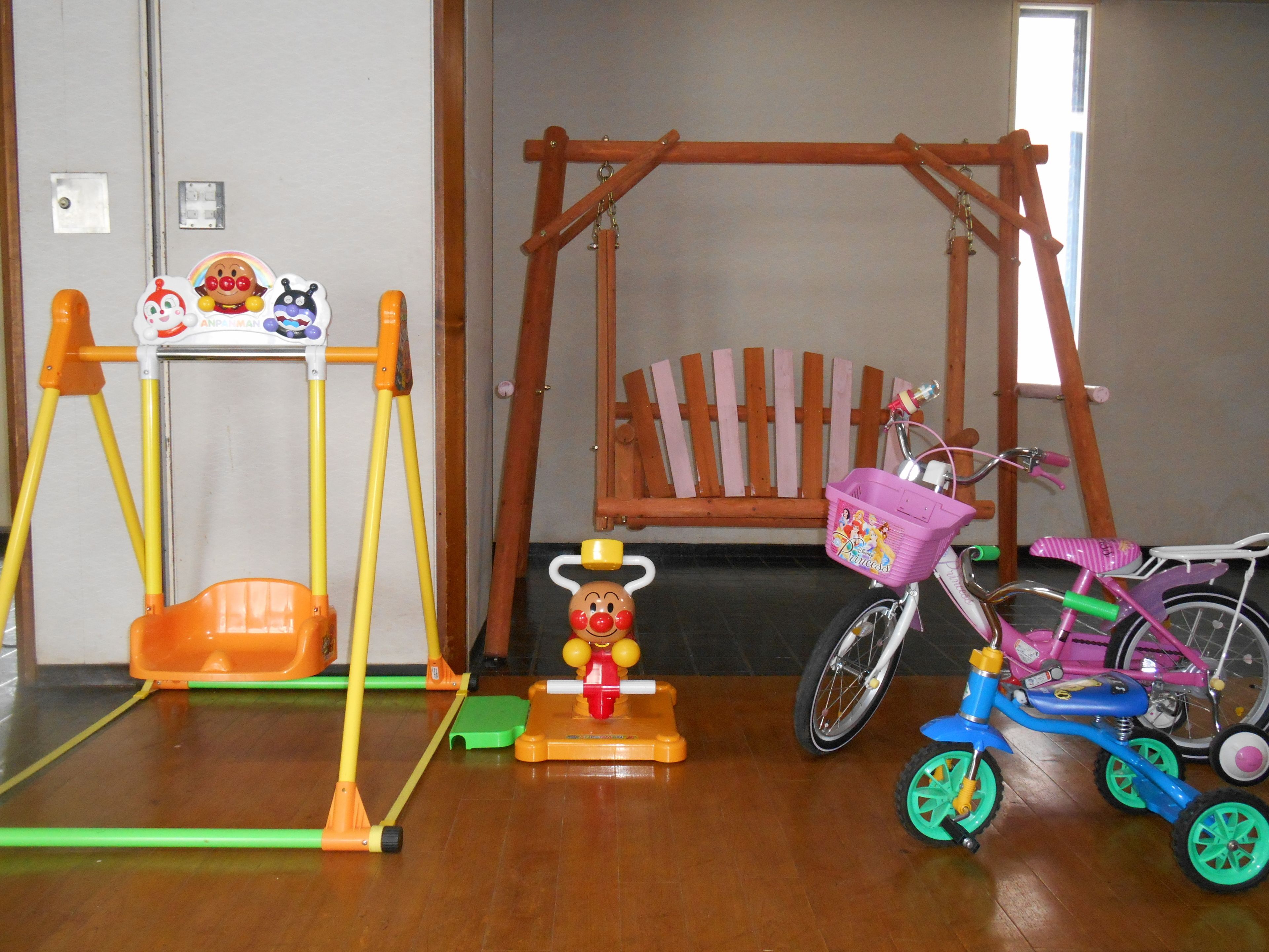 Quarto com balanço de madeira, uma mesa pequena com brinquedos e um triciclo.