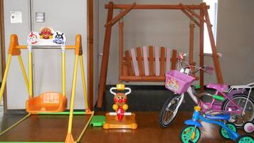Quarto com balanço de madeira, uma mesa pequena com brinquedos e um triciclo.