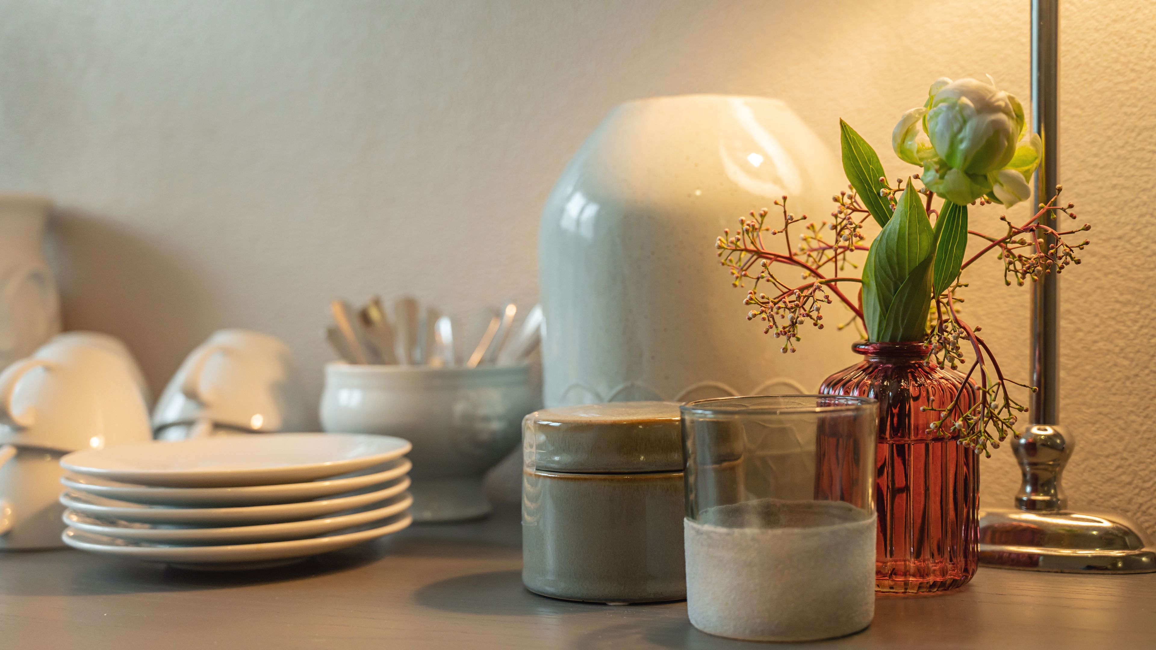 Uma mesa com pratos, um vaso com flores e vários recipientes.