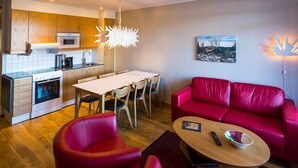Uma sala de estar moderna com um sofá vermelho, uma mesa de centro de madeira e uma área de jantar com mesa e cadeiras brancas.