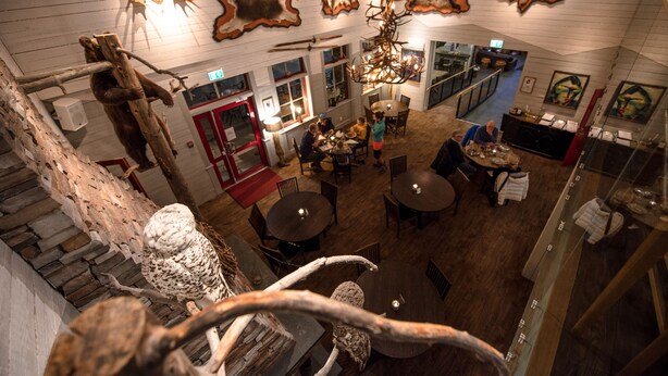 Restaurante com interiores em madeira, um candelabro e teto alto.