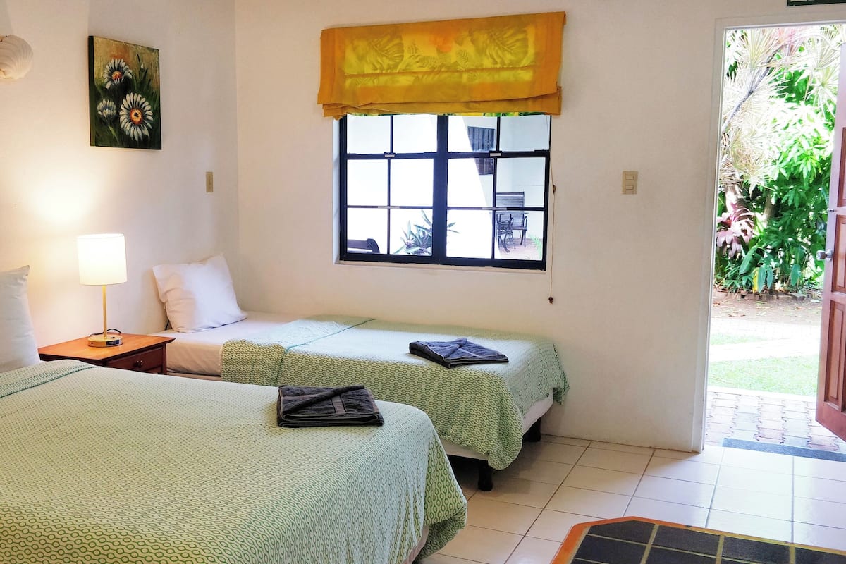 Quarto com duas camas, janela com vista para o exterior e porta que dá para um jardim.