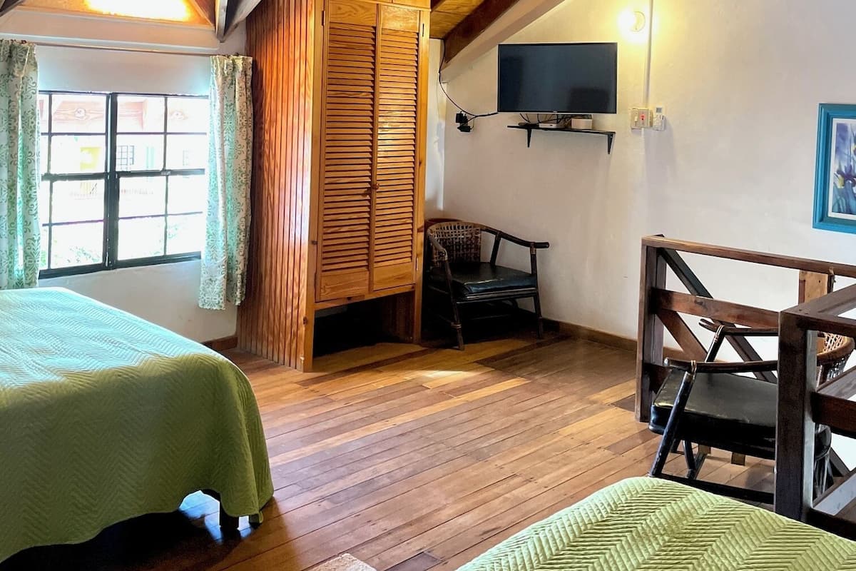 Quarto de sótão aconchegante com vigas de madeira, uma cama, uma cadeira e uma televisão.