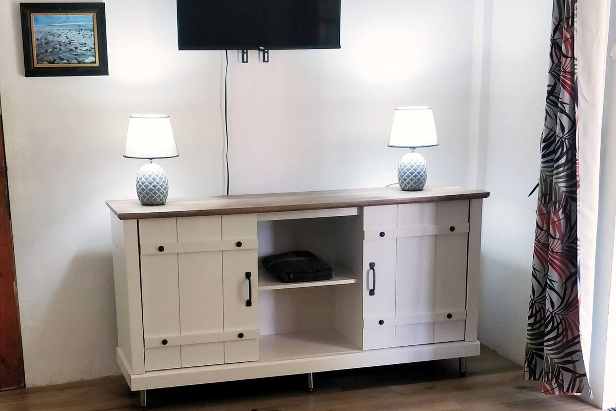 Quarto com armário branco, duas luminárias de parede, televisão de tela plana e um quadro na parede.