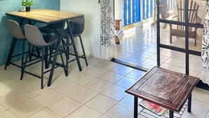 Quarto com teto de madeira, uma mesa com cadeiras, uma mesinha de centro com tampo de vidro e um sinal de saída.