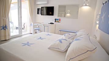 Quarto de hotel com cama, escrivaninha, cadeira, televisão e porta de correr para a varanda.
