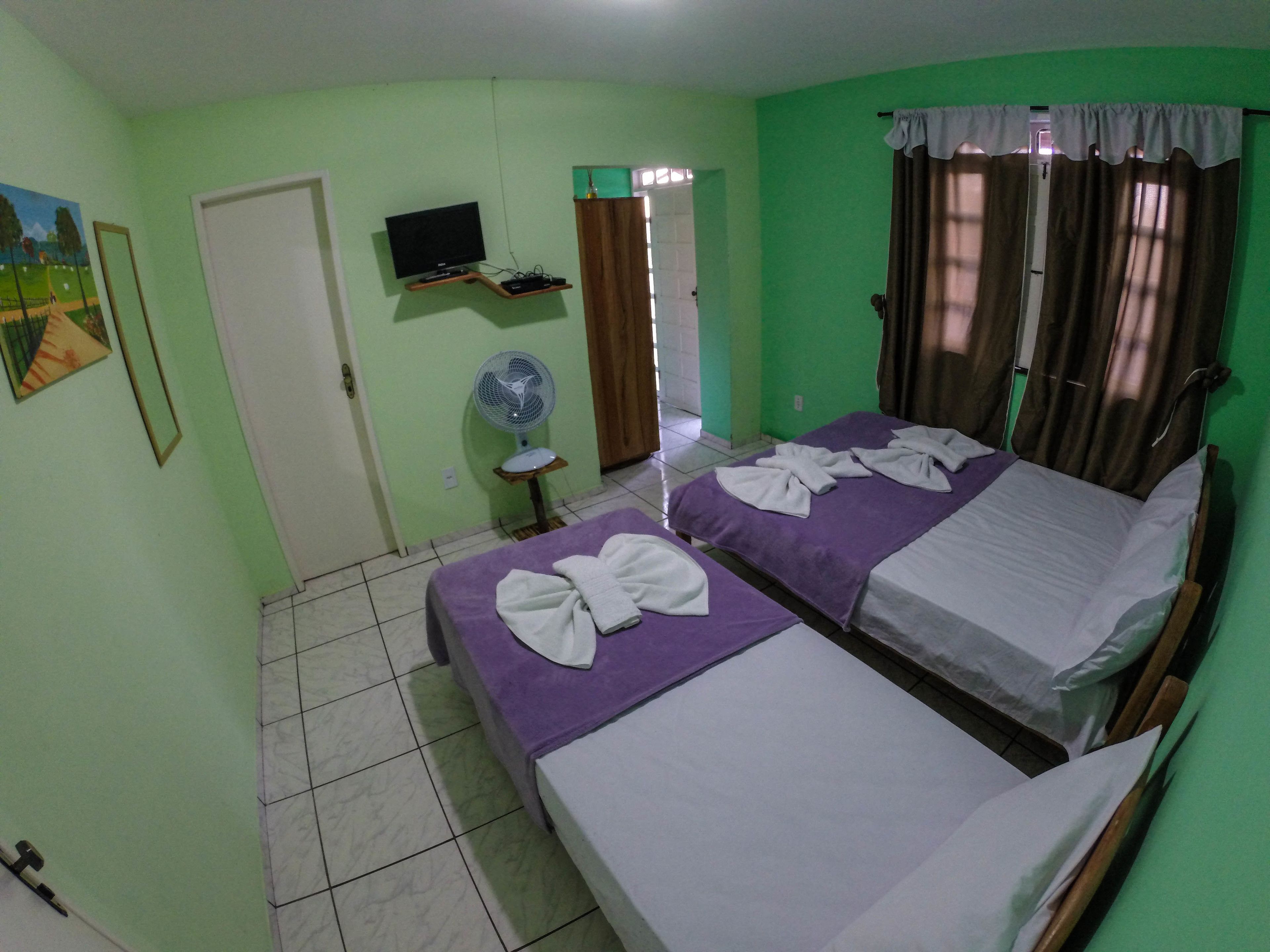 Quarto de hotel com duas camas, televisão, ventilador e porta para um banheiro.