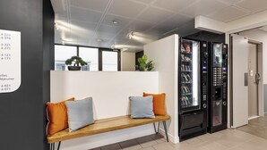 Uma área de recepção com um banco, máquinas de venda automática e uma parede com uma lista de números de quartos.