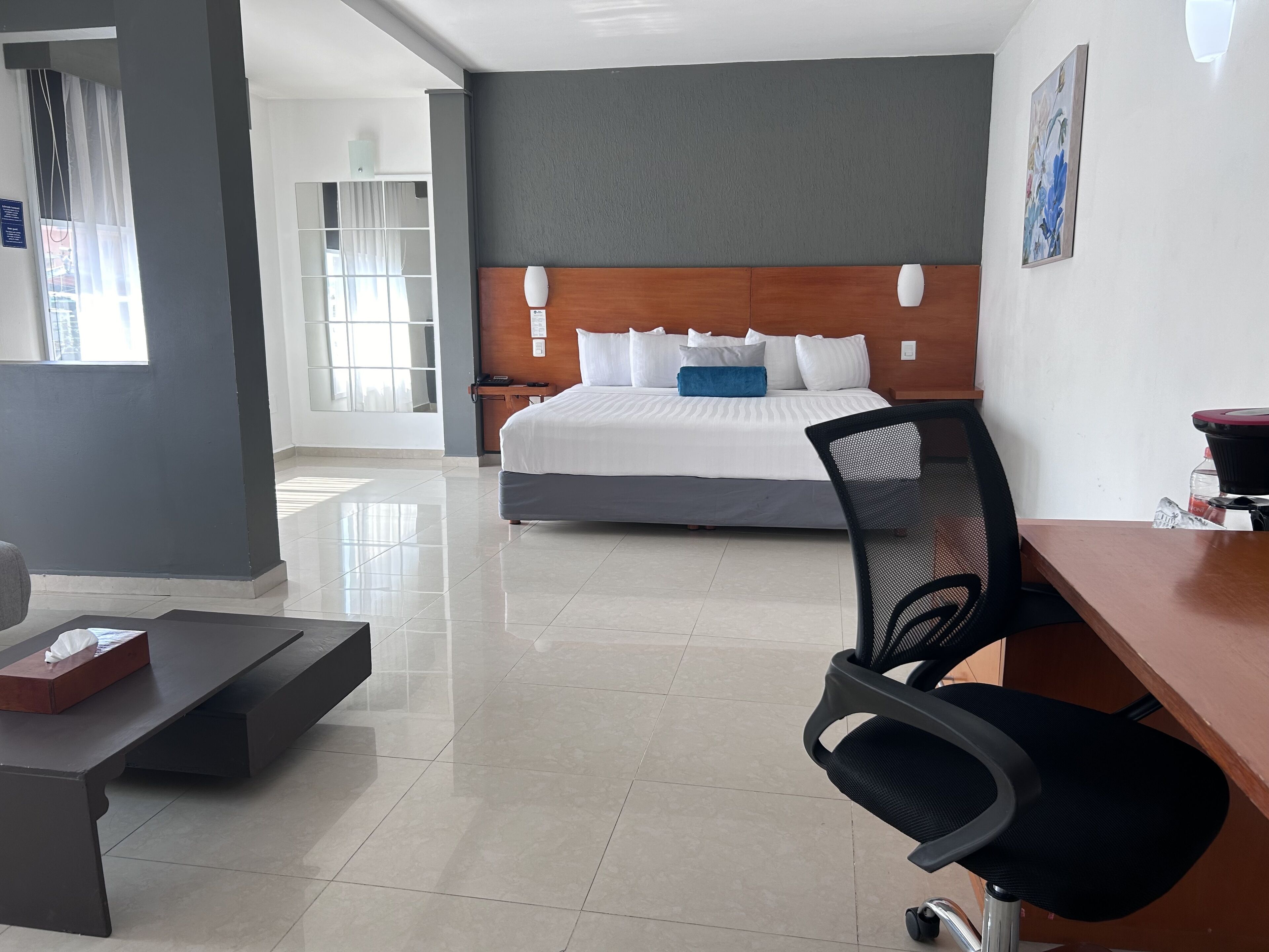 Quarto de hotel com cama, escrivaninha, cadeira e janela.