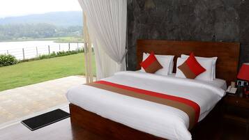 Quarto com uma cama grande, parede de pedra e vista para um lago.