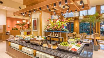 Uma área de buffet com diversos pontos de comida, um arranjo floral central e disposição de mesas.
