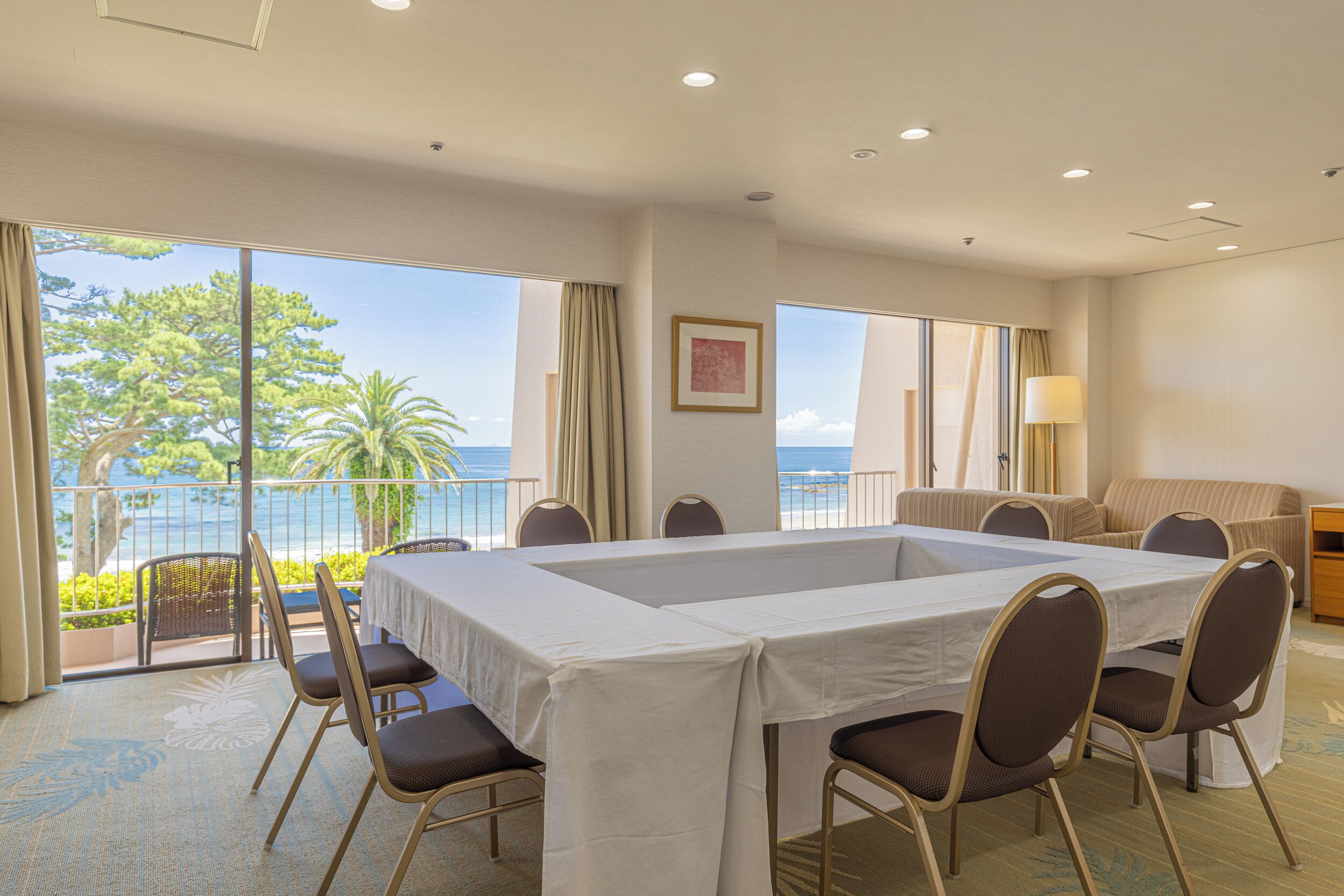 Uma sala de conferências com uma mesa grande e cadeiras, janelas amplas com vista para o oceano e uma varanda com guarda-corpo.