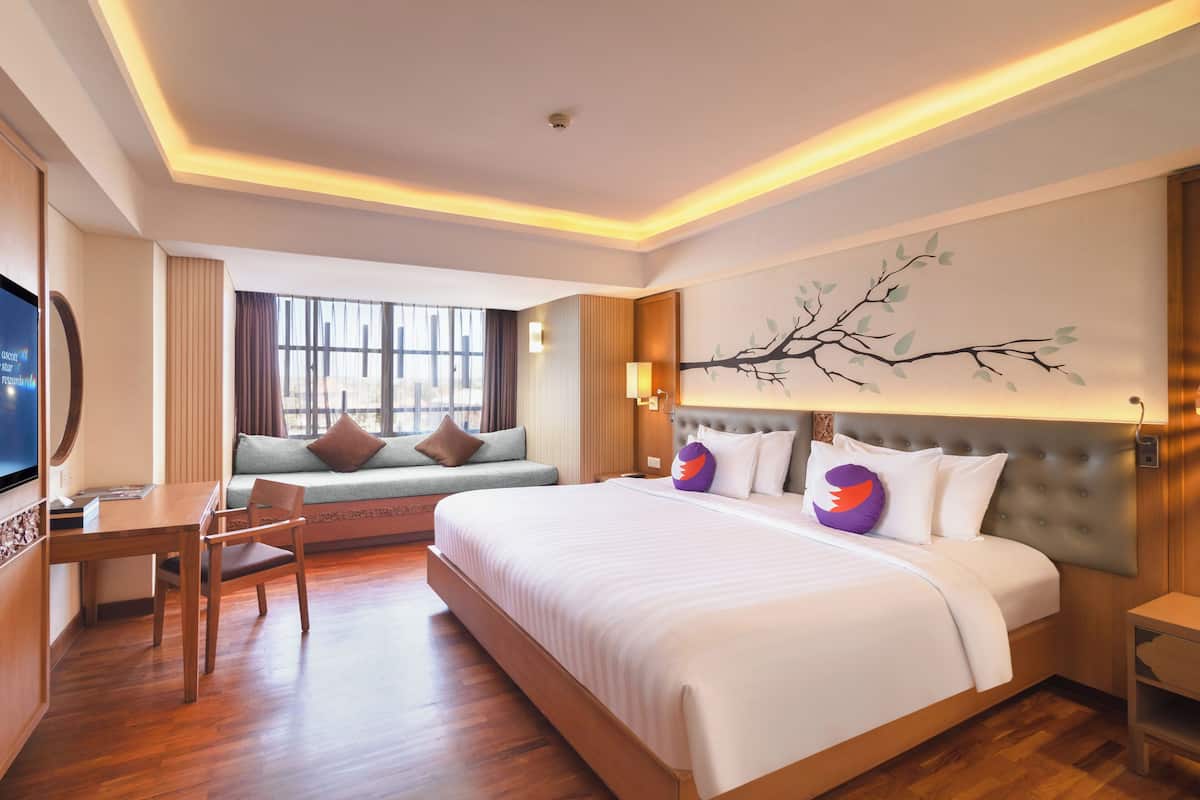 Quarto de hotel com uma cama grande, um sofá, uma escrivaninha e uma televisão.