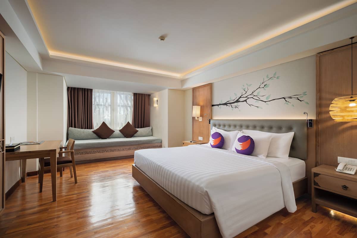 Quarto de hotel com uma cama grande, uma escrivaninha, uma cadeira, um sofá e uma luminária fixada na parede.