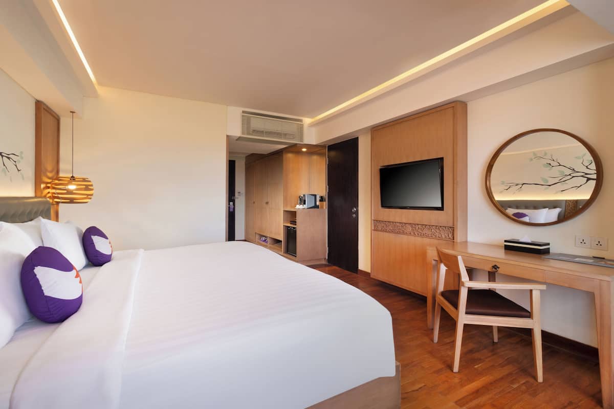 Quarto de hotel com uma cama, escrivaninha, cadeira, televisão e espelho.