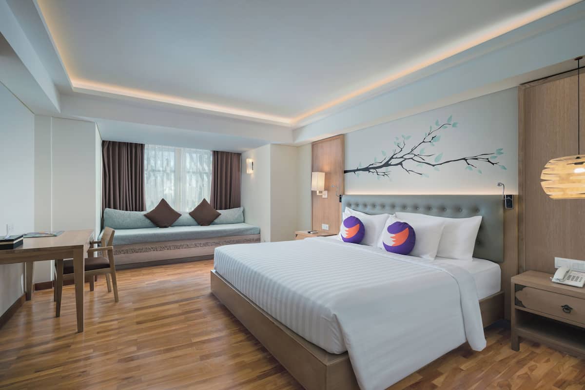 Quarto de hotel com cama, sofá, escrivaninha e janela com cortinas.