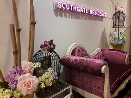 Um sofá roxo aconchegante, uma gaiola de pássaro preta com flores e uma placa de neon que diz "SOUTHGATE RESIDENCE".