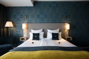 Quarto de hotel com uma cama grande, duas luminárias de cabeceira, um encosto de cama e uma parede azul escura com padrão.