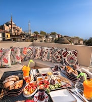 Uma área de refeições no terraço com vista para edifícios históricos, variedade de comidas e uma mesa posta para dois.