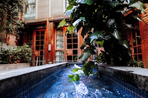 Piscina com borda azulejada, rodeada por um edifício de madeira com janelas e portas emolduradas a vermelho.