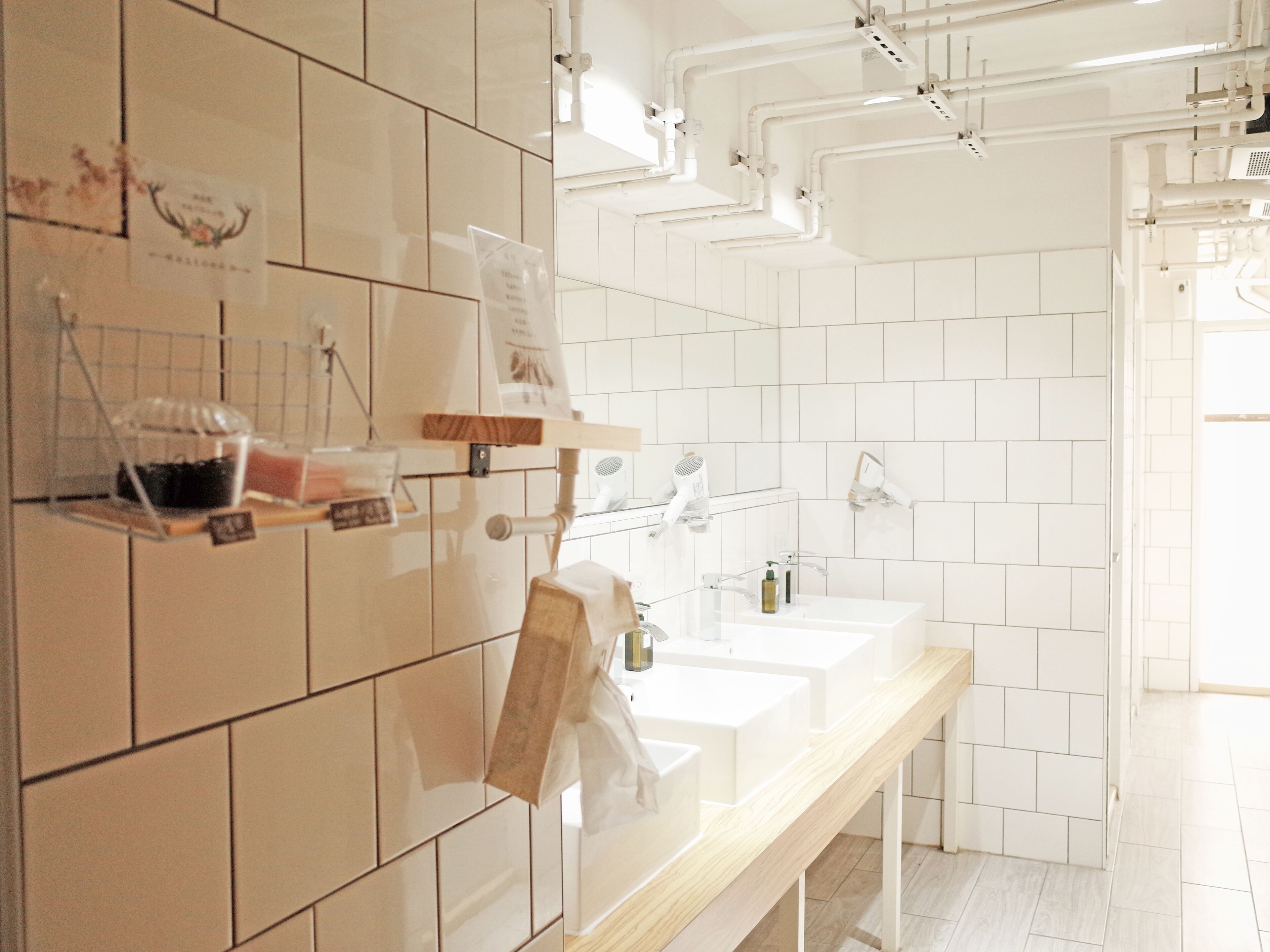 Um banheiro moderno com azulejos brancos, toucador de madeira e secador de cabelo fixado na parede.