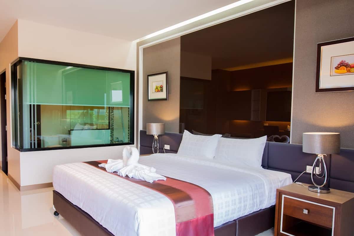 Quarto de hotel moderno com uma cama grande, uma mesinha de cabeceira com luminária, um espelho e vista para o banheiro.