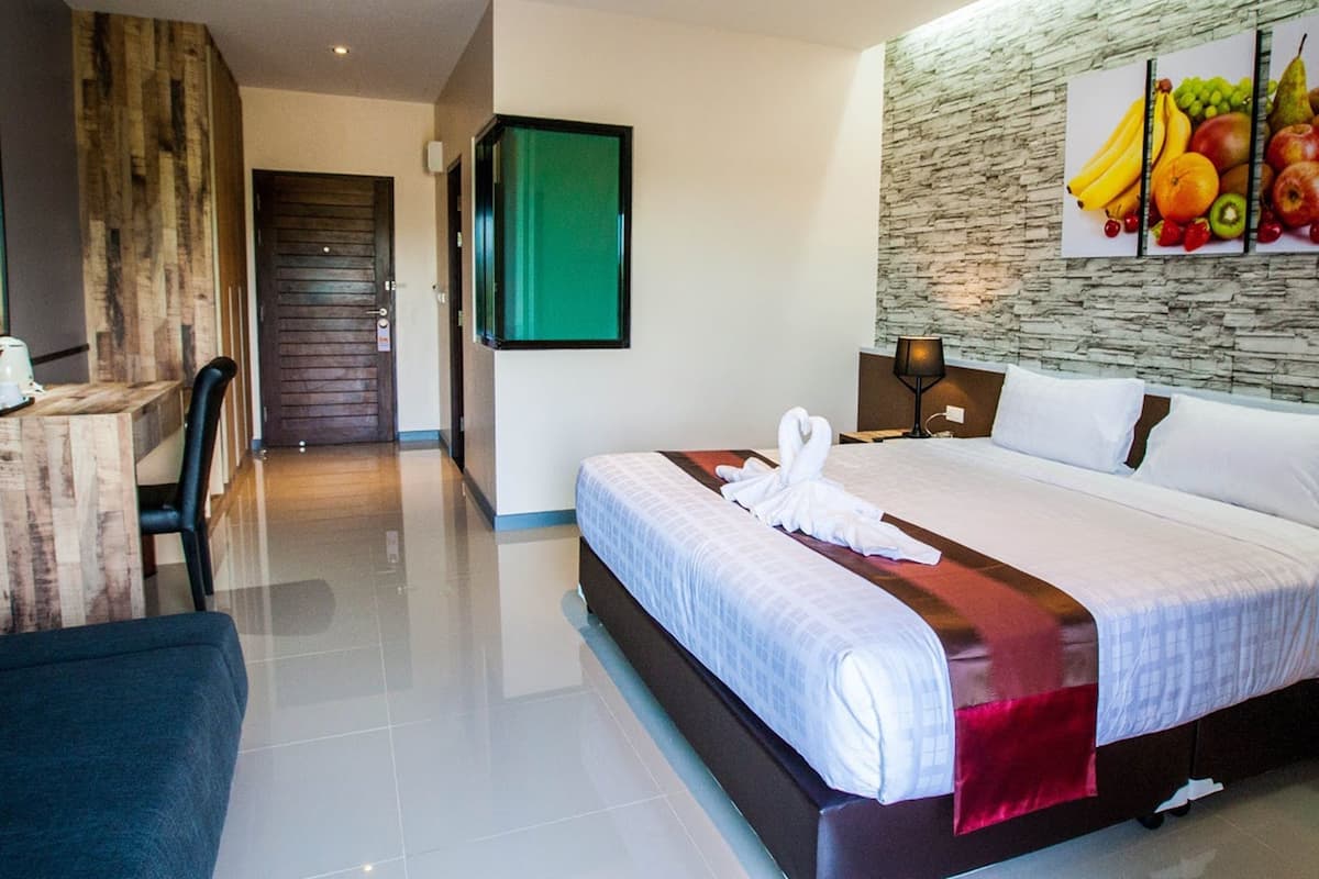 Quarto de hotel com cama, escrivaninha, cadeira, porta verde e parede com pintura de frutas.