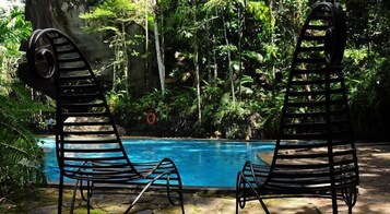 Duas cadeiras de descanso pretas à beira de uma piscina, com paisagem tropical ao fundo.