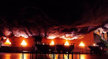 Um restaurante subterrâneo com mesas e cadeiras, iluminado por luz de velas.