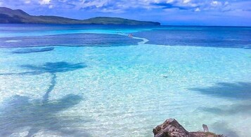 Vista clara de uma praia com águas rasas e uma cordilheira ao longe.