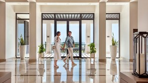Um hall de hotel moderno com piso refletivo, janelas amplas e plantas em vasos.