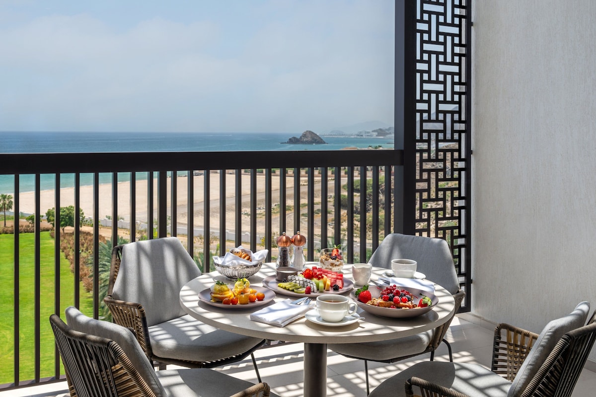 Varanda com mesa posta para o pequeno-almoço, com vista para uma praia e campo de golfe.