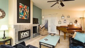 Uma sala de estar com lareira, piano, sofá e mesa de centro.