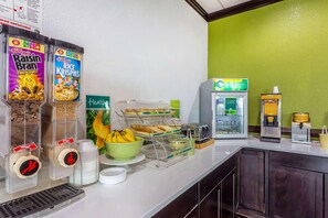 Uma mesa de pequeno-almoço com cereais, máquina de café, dispensador de sumo e torradeira.