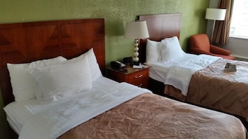 Quarto de hotel com duas camas, uma mesa de cabeceira com abajur e uma cadeira.