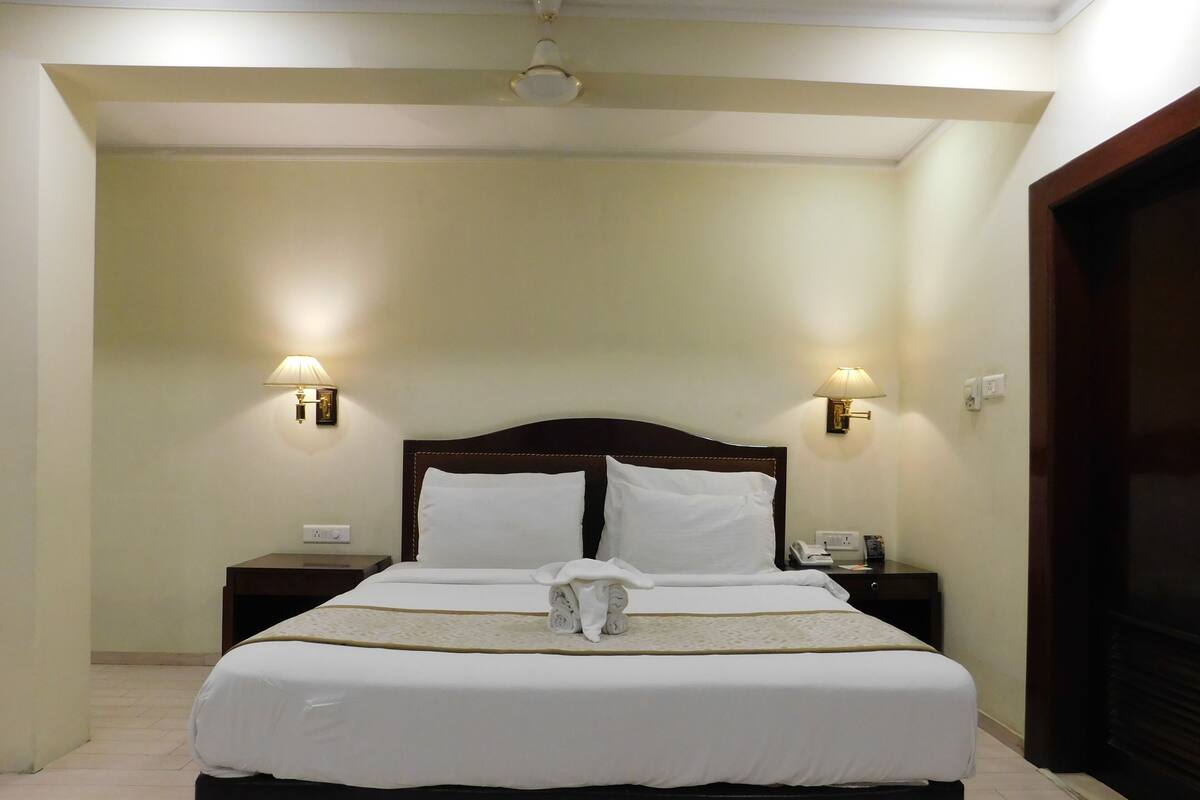 Cama bem arrumada com lençóis brancos, duas luminárias de cabeceira e cabeceira de madeira.