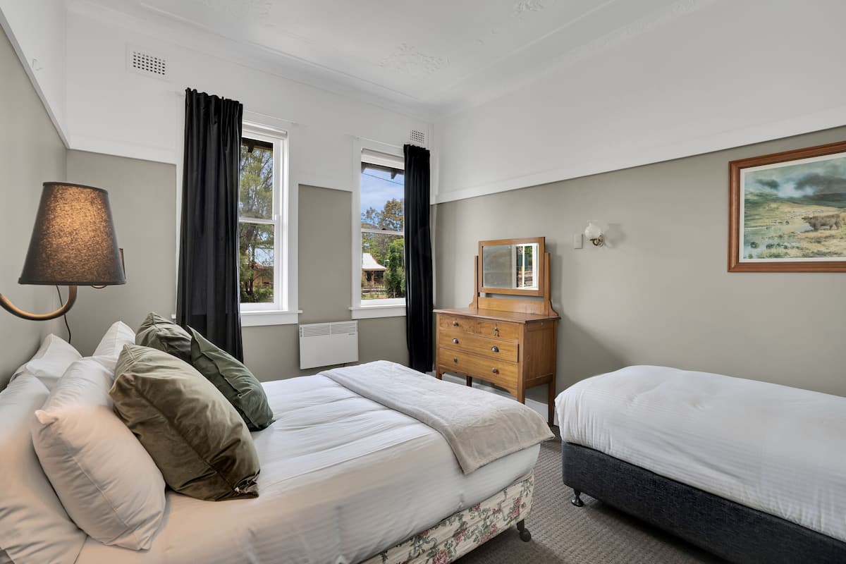 Quarto com cama, penteadeira, abajur, janela e um quadro na parede.