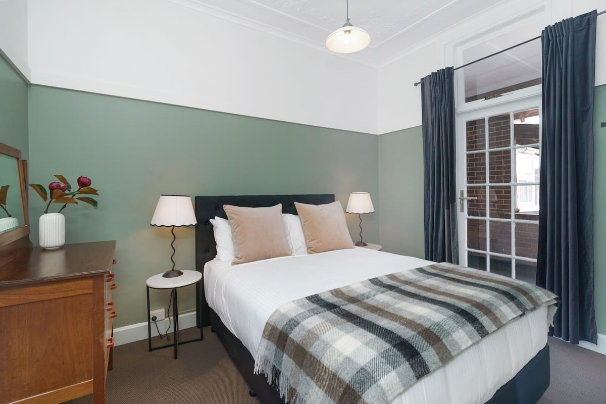 Quarto com cama, abajures, cômoda e janela com cortinas.