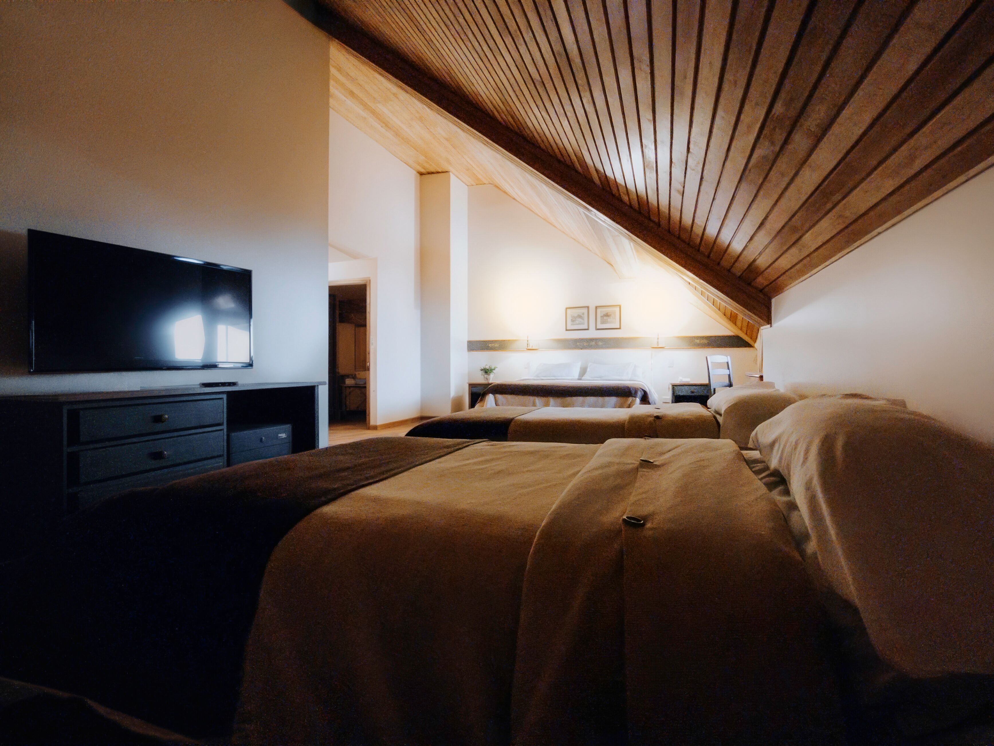 Quarto com televisão, escrivaninha e duas camas.