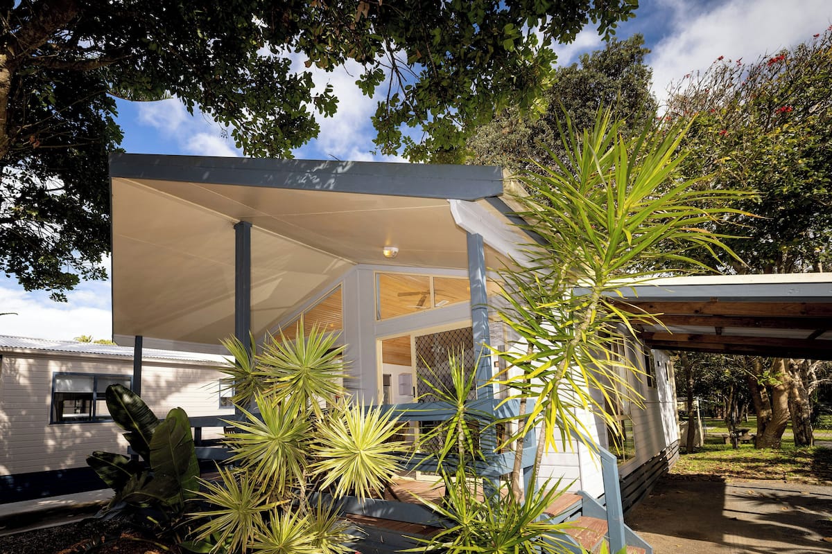 Uma casa moderna com varanda coberta, rodeada por diversas plantas tropicais.