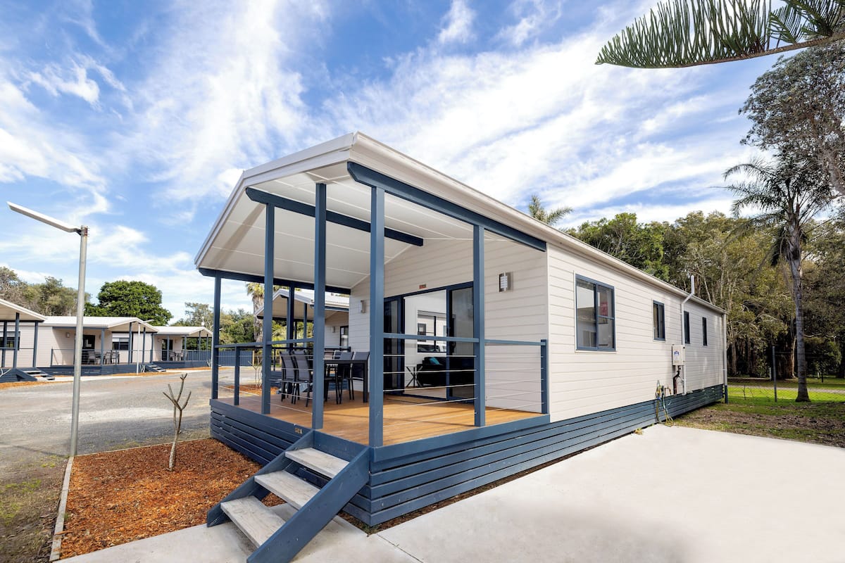 Uma casa móvel moderna com varanda coberta, um pequeno espaço de estar ao ar livre e um caminho de acesso de concreto.