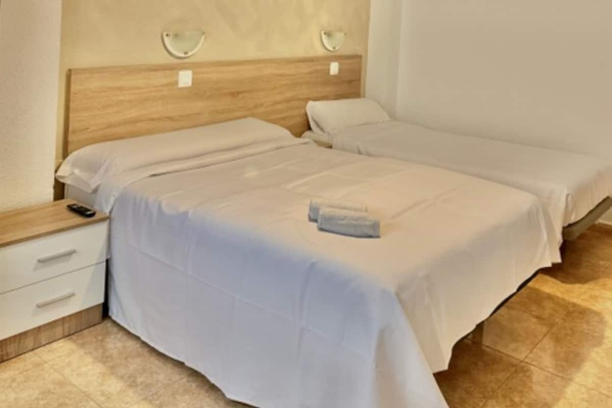 Quarto com duas camas, mesa de cabeceira com abajur e luminária no teto.