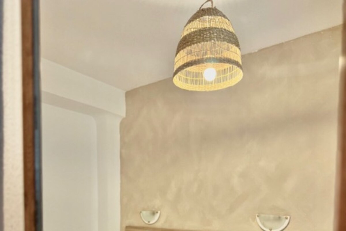 Quarto de hotel com duas camas, cabeceira de madeira e luminária pendente.