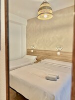 Quarto de hotel com duas camas, cabeceira de madeira e luminária pendente.