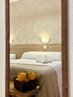 Quarto de hotel com cama, mesa de cabeceira com cesta de frutas e luminárias na parede.