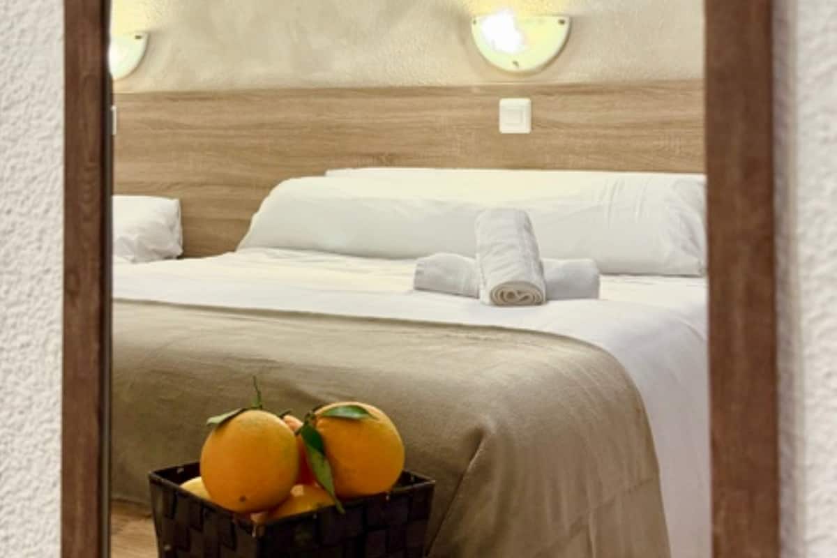 Quarto de hotel com cama, mesa de cabeceira com cesta de frutas e luminárias na parede.
