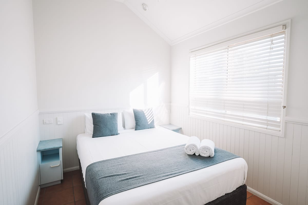 Um quarto com uma cama, uma mesa de cabeceira, uma janela com persianas e uma toalha sobre a cama.