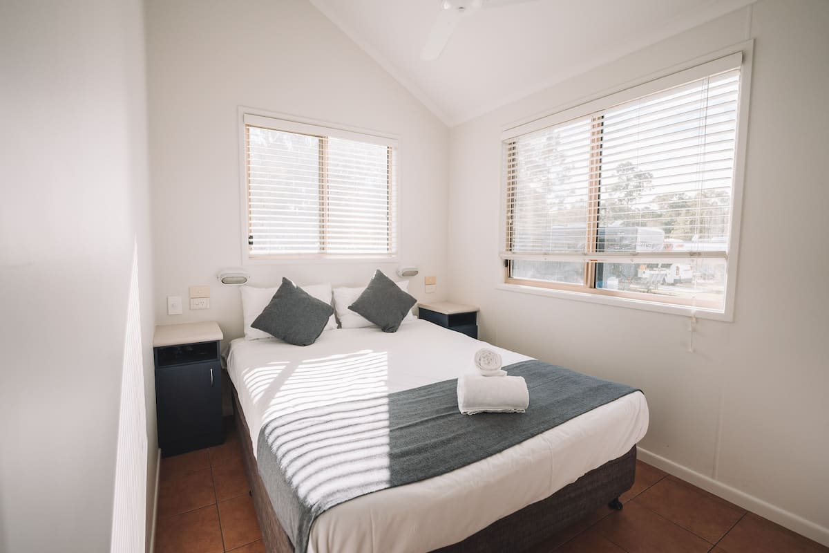 Quarto com uma cama, duas mesas de cabeceira, uma janela e um ventilador de teto.